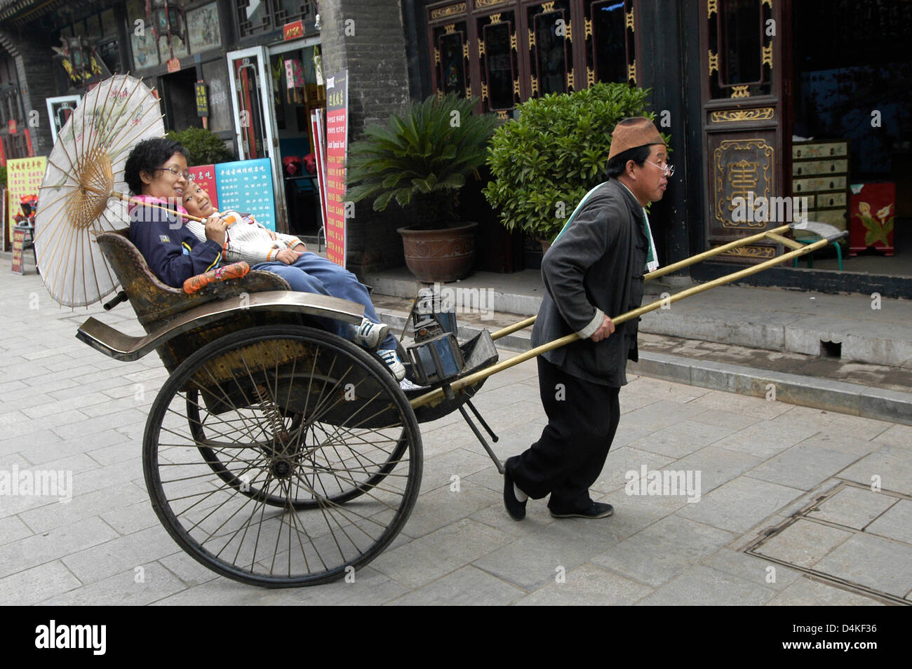 A rickshaw driver carries passengers through the old streets of Pingyao ...