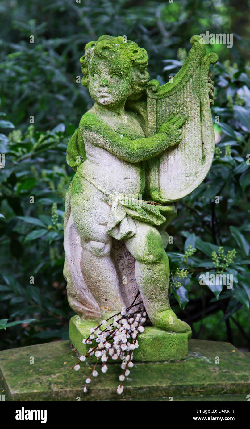 A figure of a harp playing angel, partly overgrown with moss, is ...