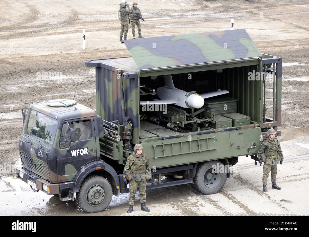 Soldiers stand in front of a lorry which is loaded with a small ...