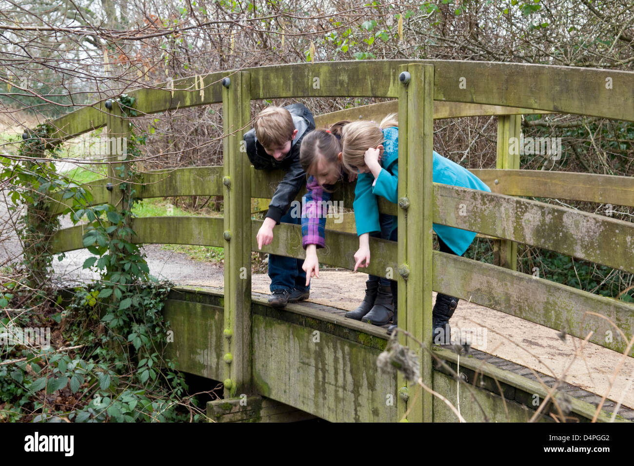 Three Caucasian children leaning over foot bridge and pointing at ...