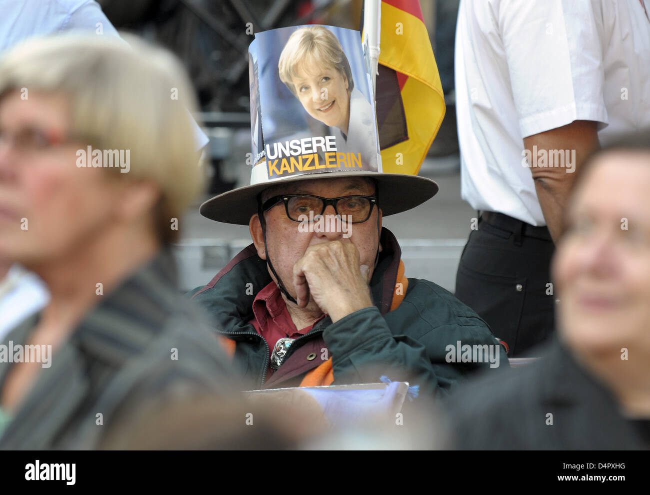 A man wearing a hat decorated with pictures of Angela Merkel attends an ...