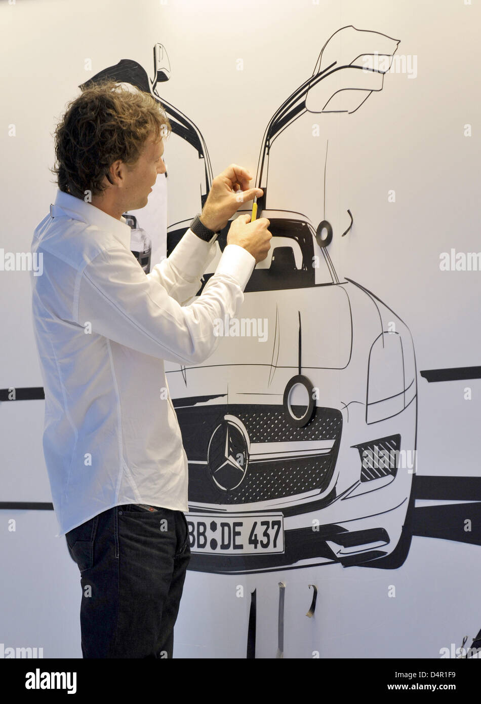 A graphic artist tapes the silhouette of a Mercedes SLS AMG to a wall ...