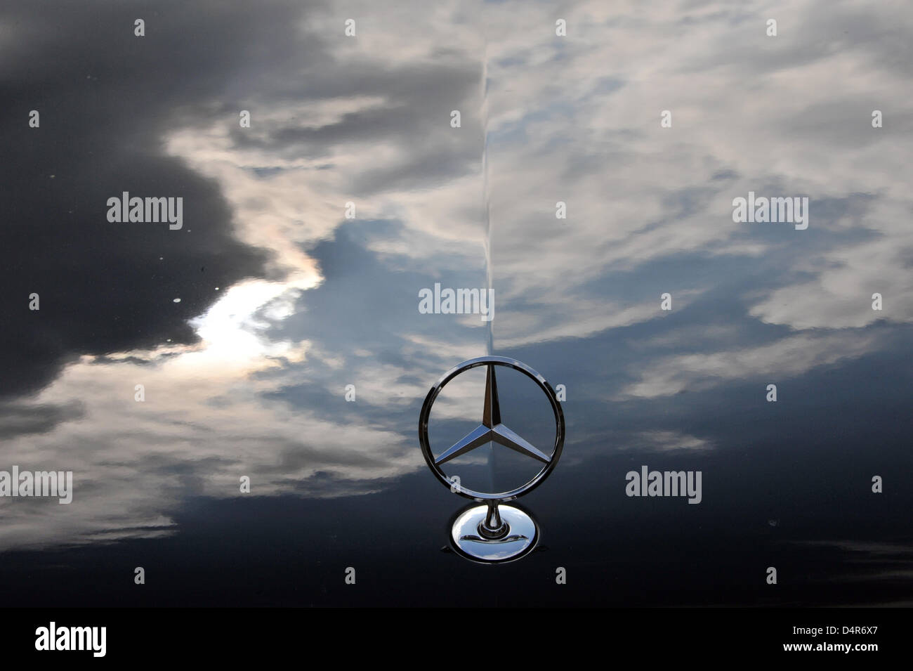 A Mercedes-Benz star in front of a cloudy sky reflecting on the hood of ...