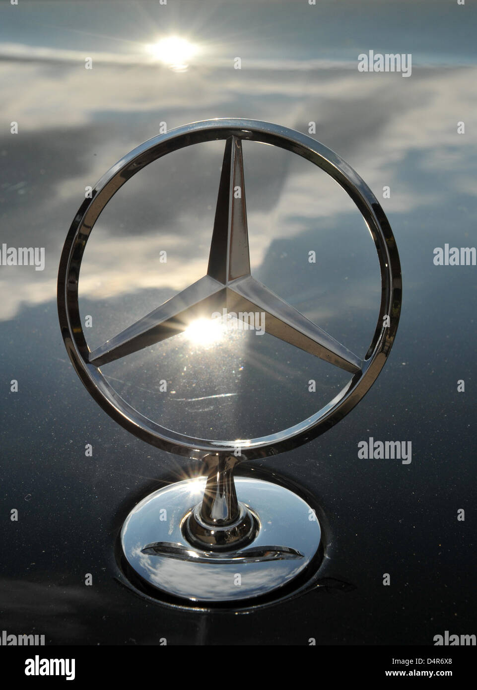 A Mercedes-Benz star in front of a cloudy sky reflecting on the hood of ...