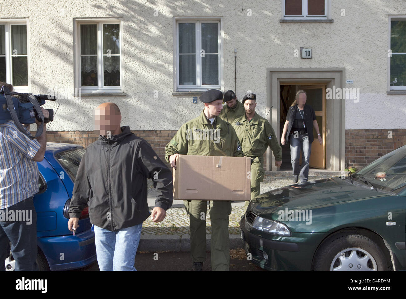 Police officers carry a box with things they seized while searching the ...