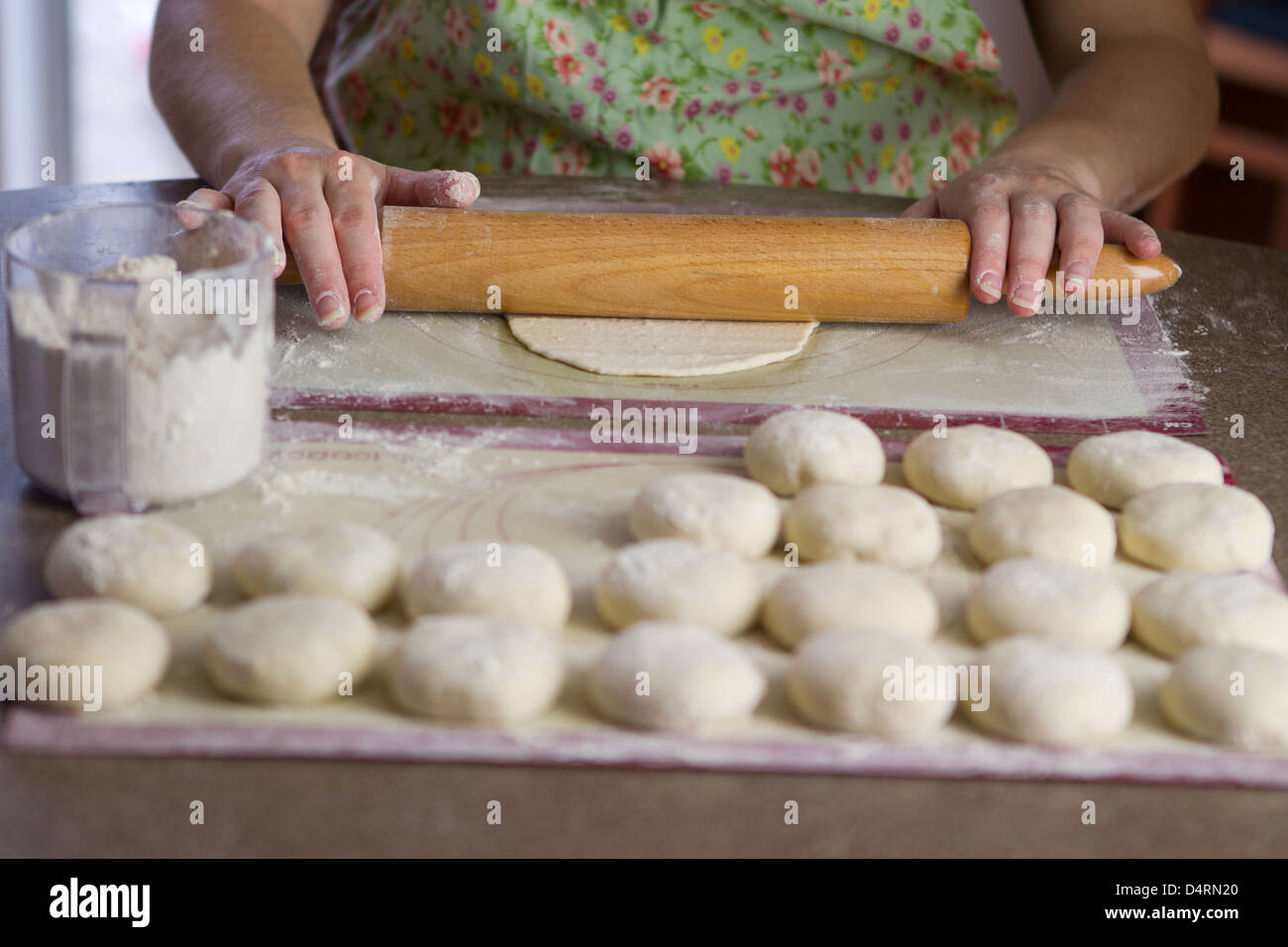 A lady flatten the dough to make flat bread pizzas using classic wooden ...