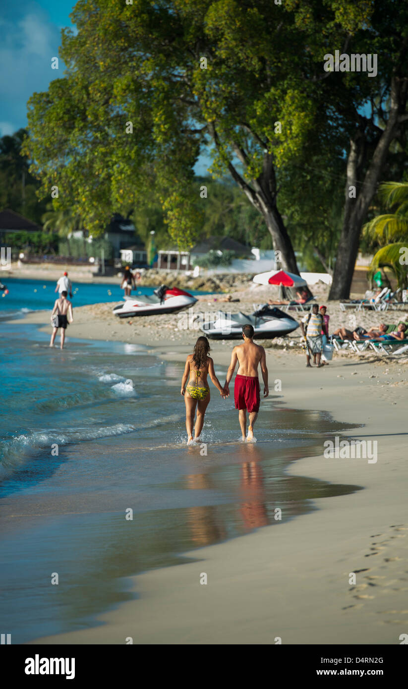 a couple walk along a palm fringed beach near Holetown, Parish of St ...