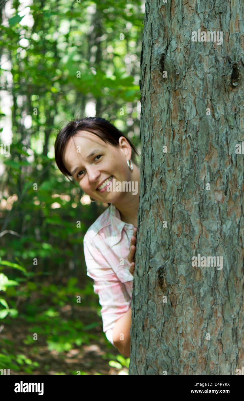 Young woman peeking from behind a tree Stock Photo - Alamy