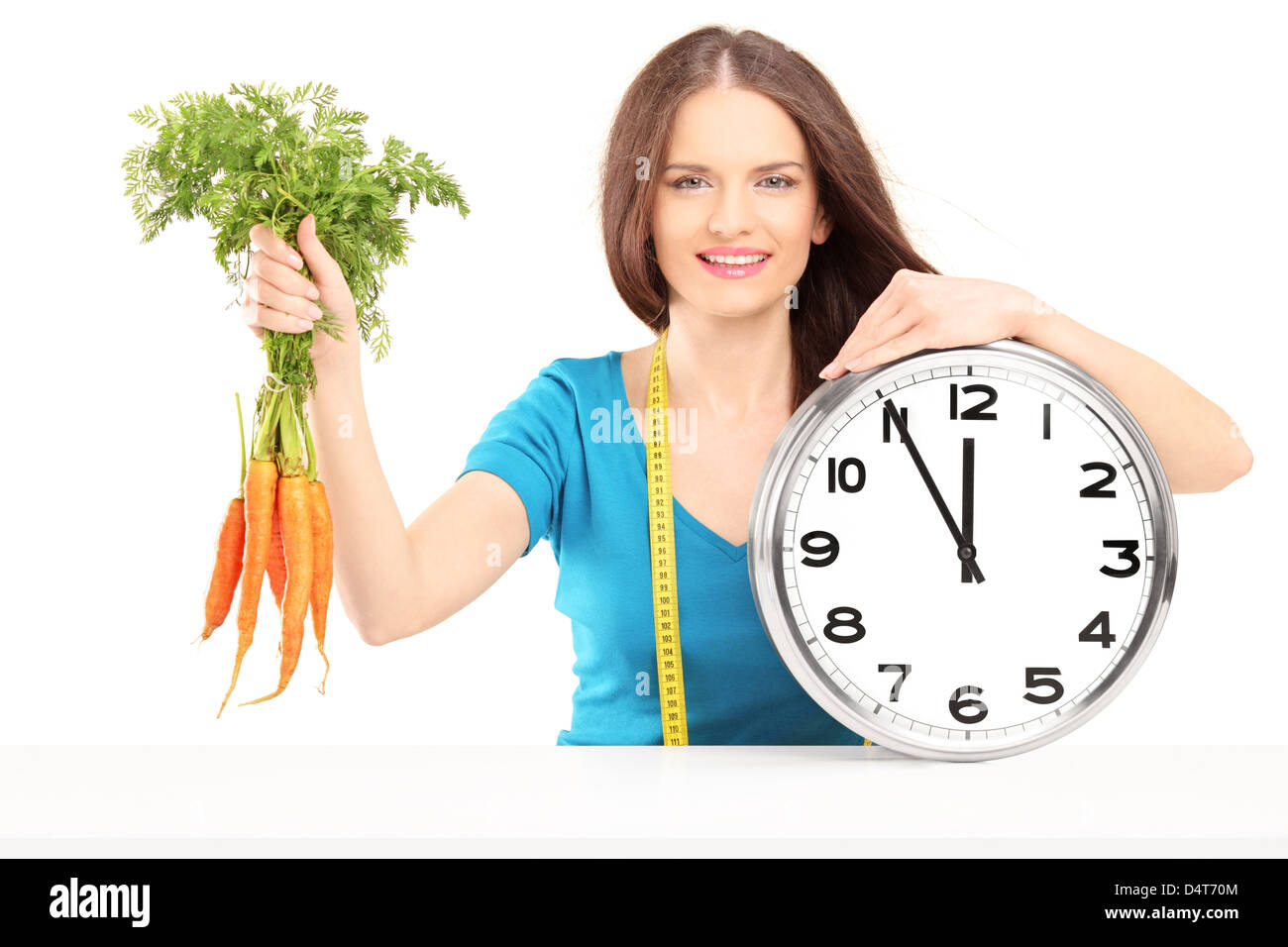 Young woman with measuring tape holding carrots and a wall clock ...