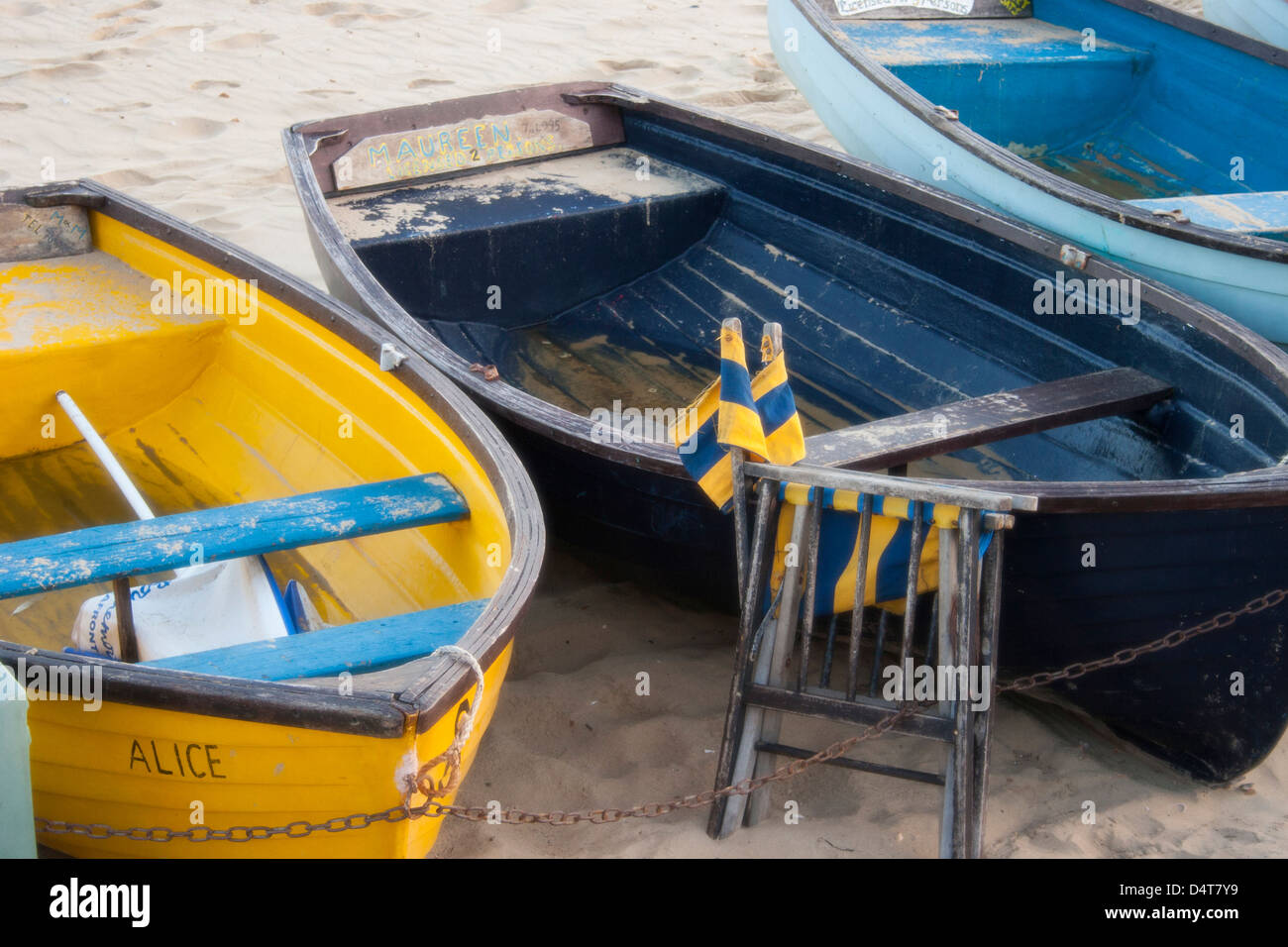 Three boats sat on the beach. A yellow boat, a dark blue boat and light ...