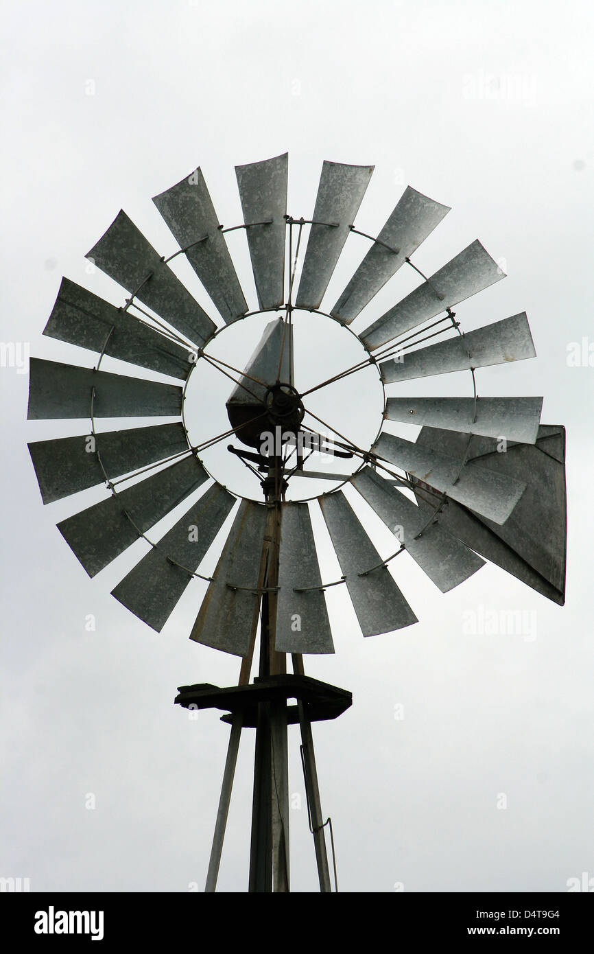 A small windmill with blades and a fin on top of a tower in a field in ...