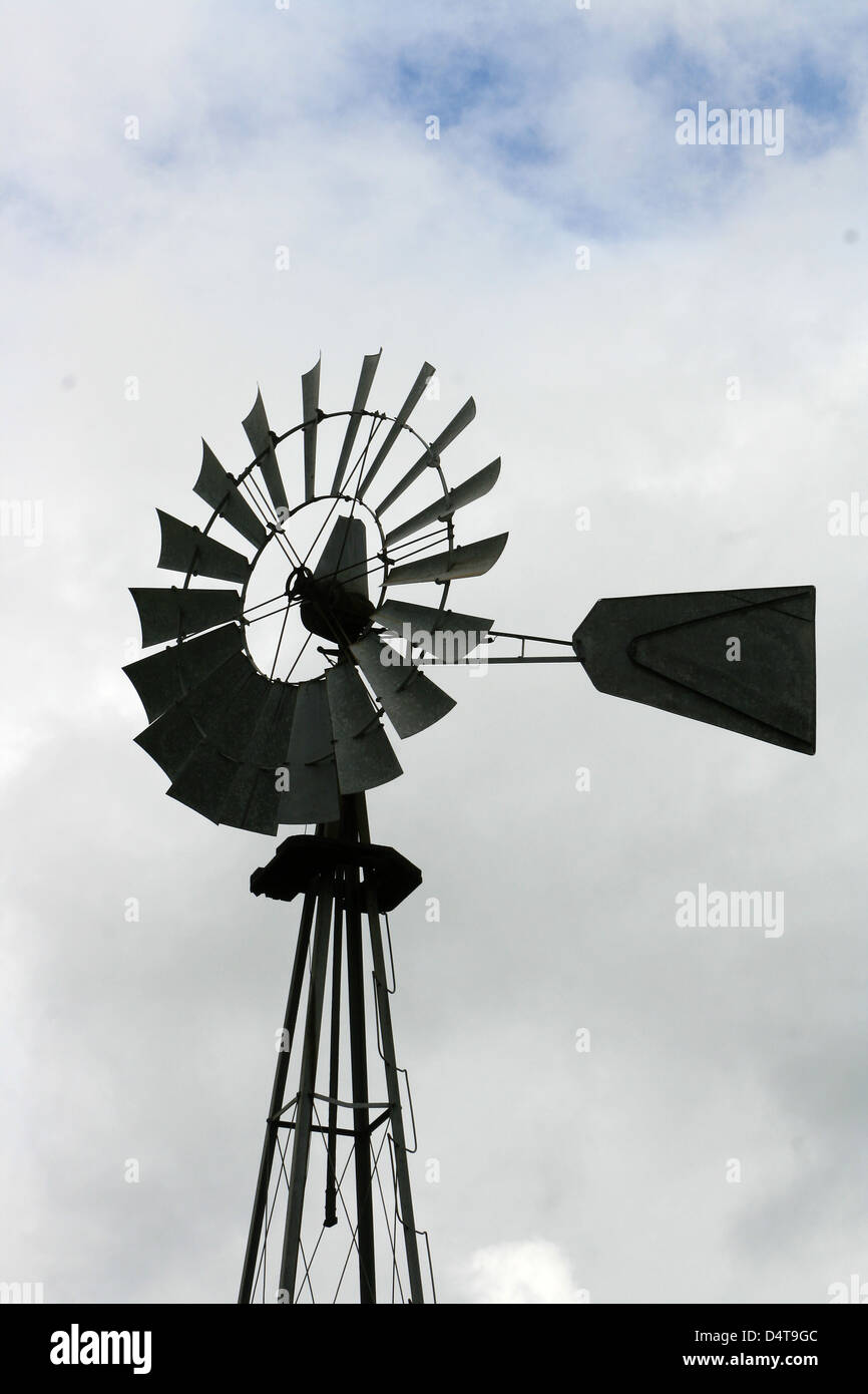 A steel windmill with blades and a fin on top of a small tower in a ...
