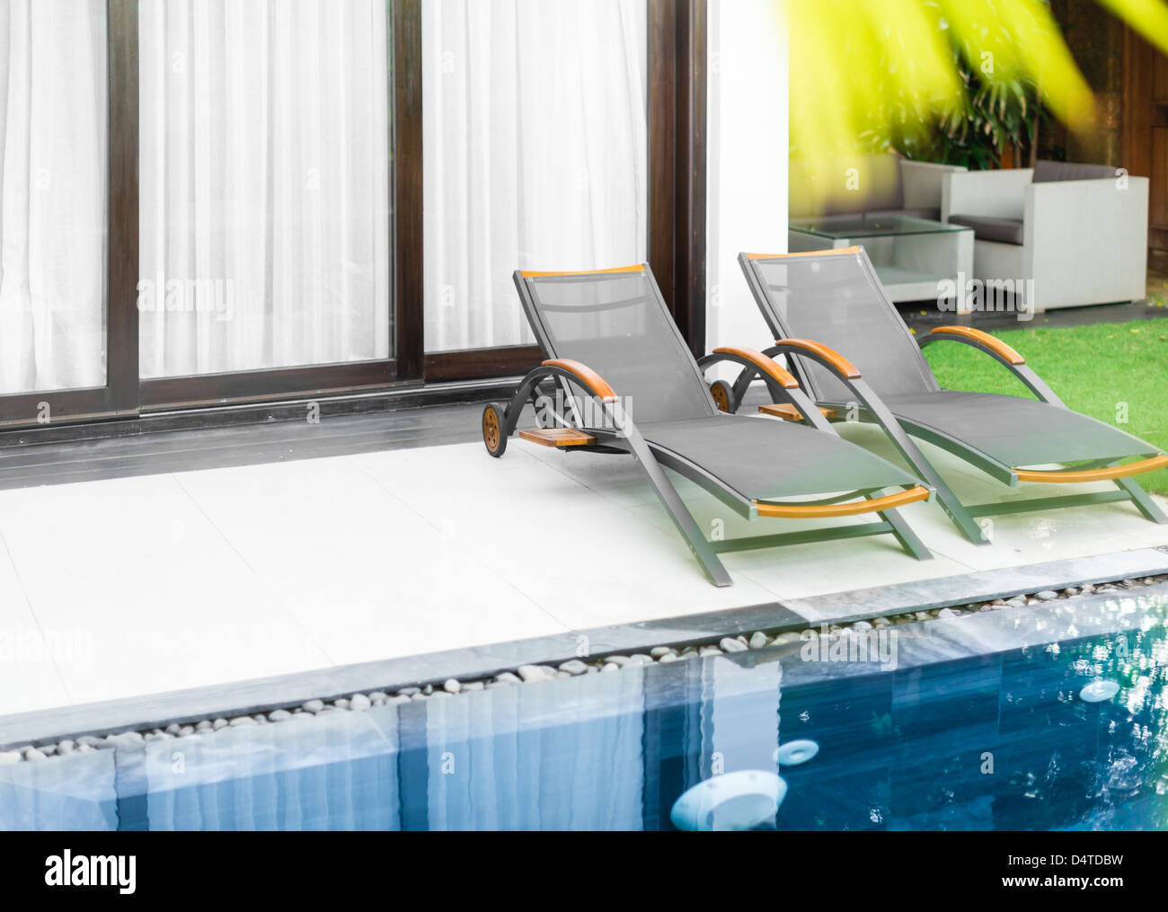 Two sunbeds on white floor and windows with curtains behind. Green lawn ...