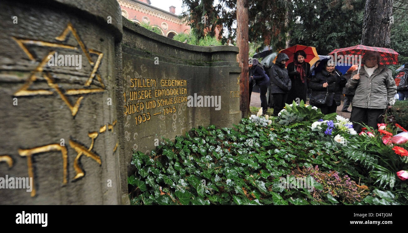 A group of people stands at a memorial stone at the Jewish Cemetery in ...