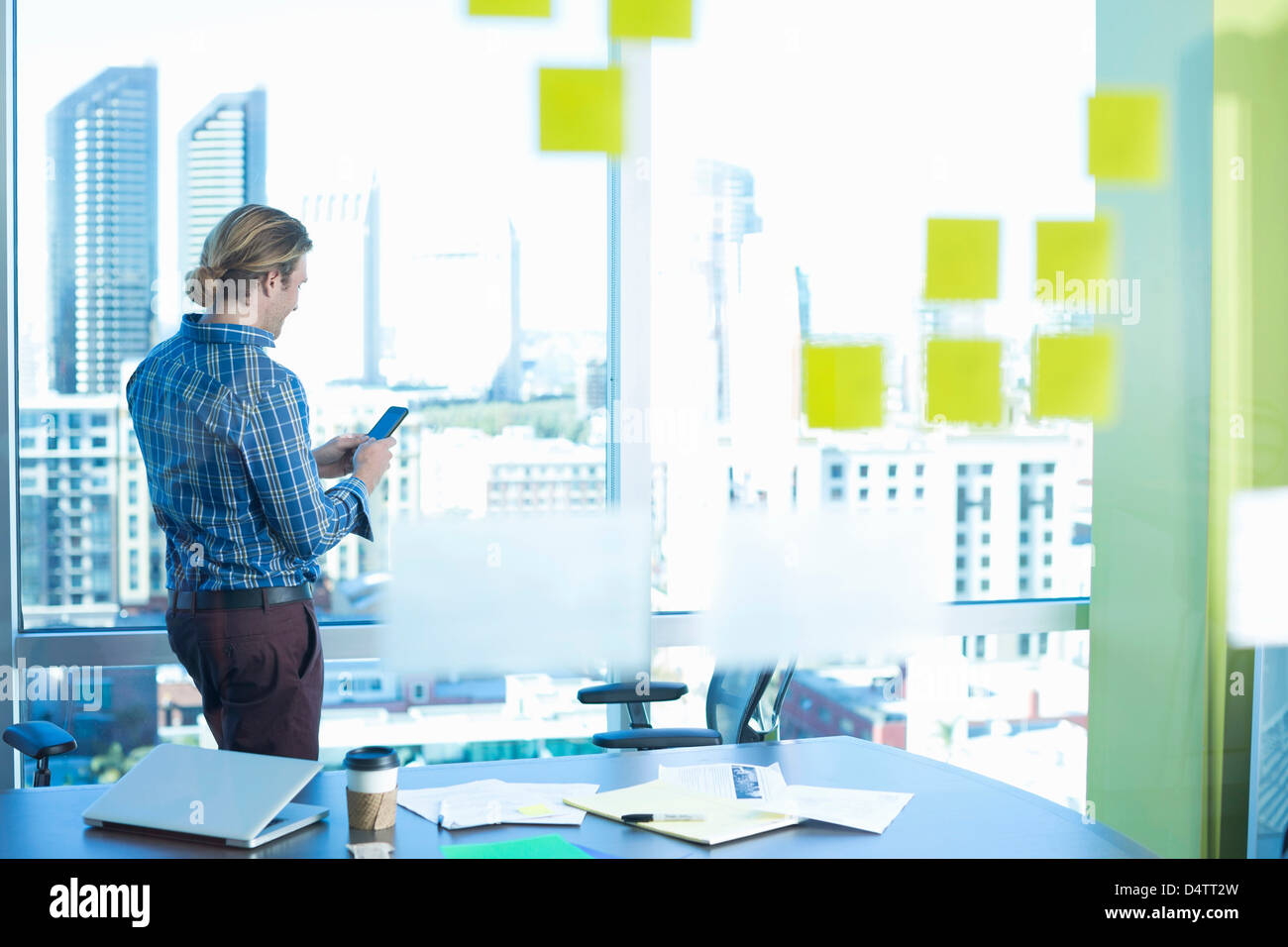Businessman using cell phone at window Stock Photo - Alamy