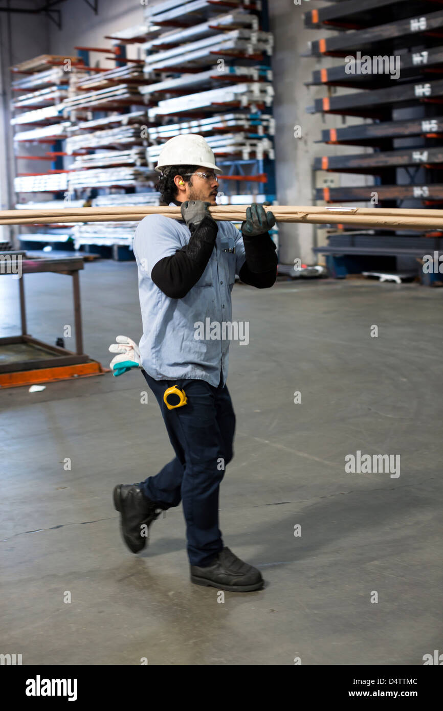 Worker carrying pipes in metal plant Stock Photo - Alamy