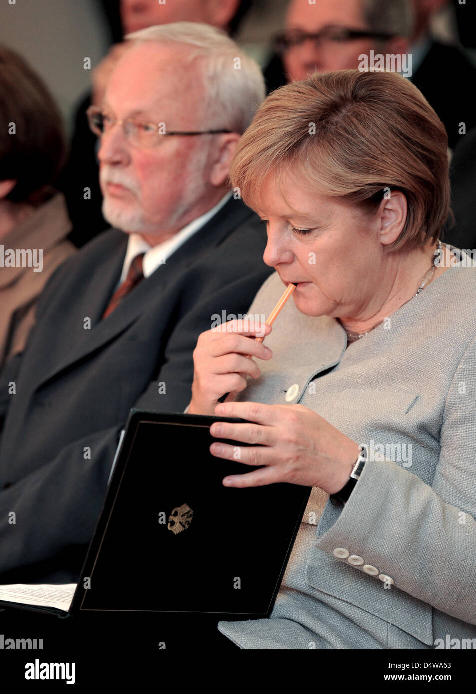 German Chancellor Angela Merkel holds a pen and sits next to first ...