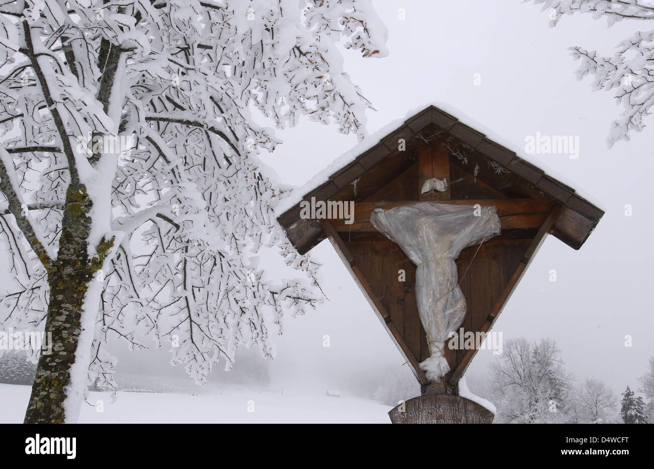A Jesus figure stands in snow and is protected with a plastic cover in ...