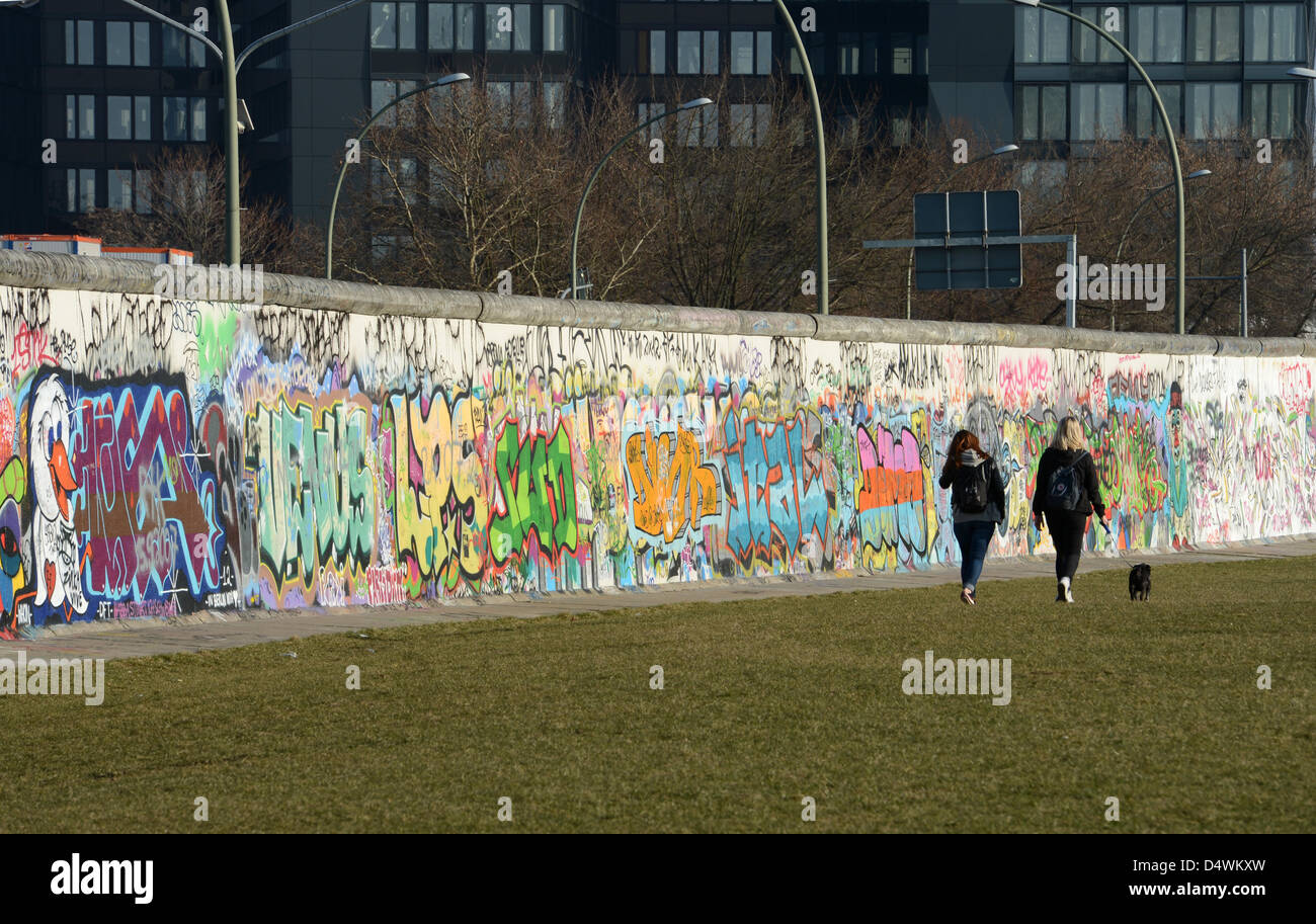People go for a walk along a section of the Berlin Wall decorated with ...