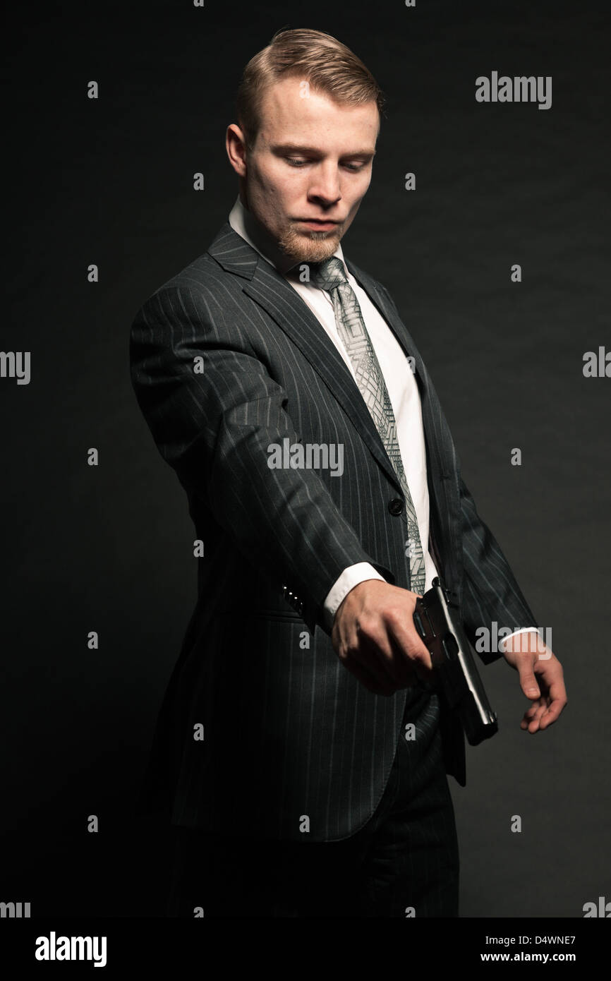 Man in suit shooting with gun. Studio shot against black Stock Photo ...