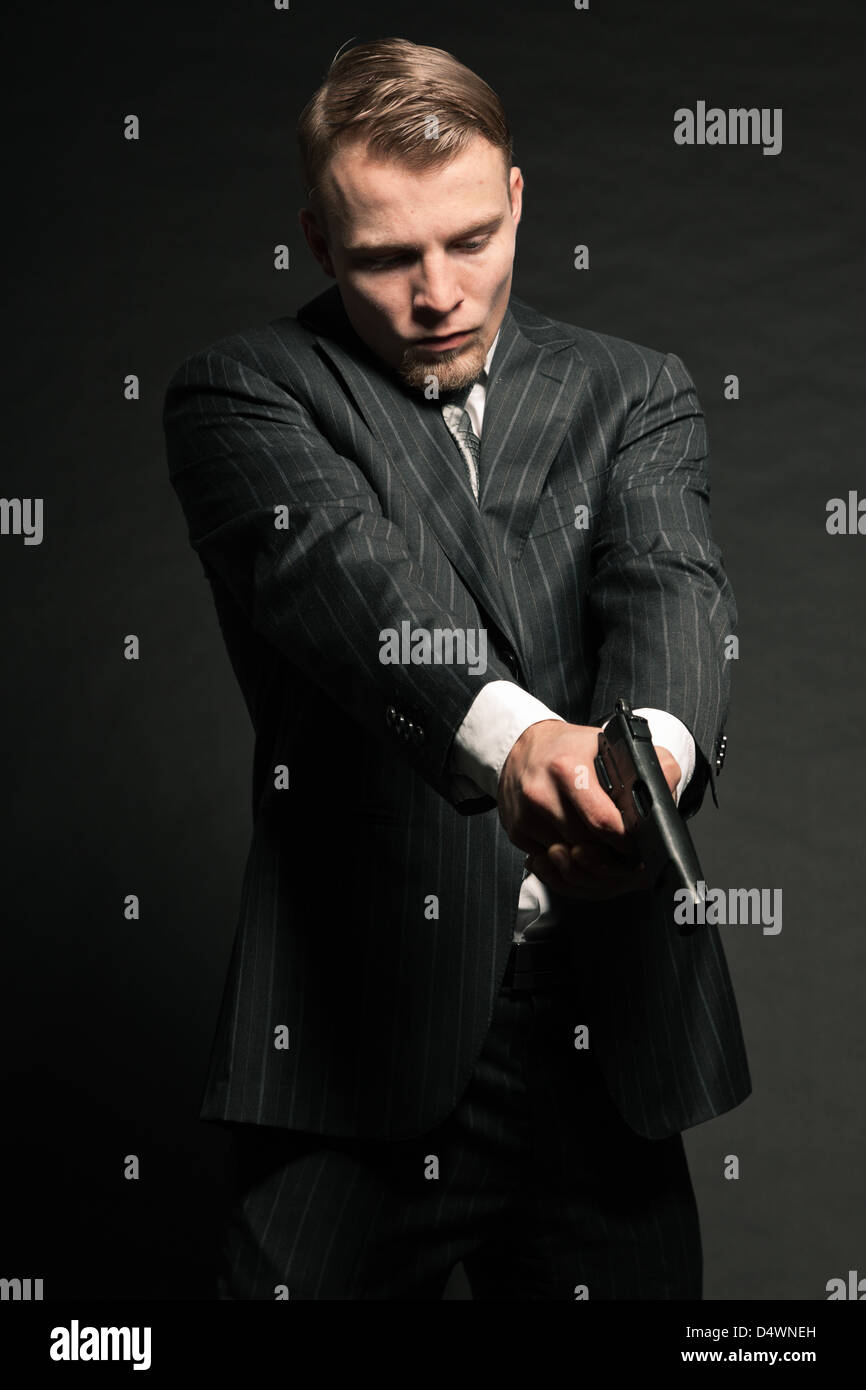 Man in suit shooting with gun. Studio shot against black Stock Photo ...