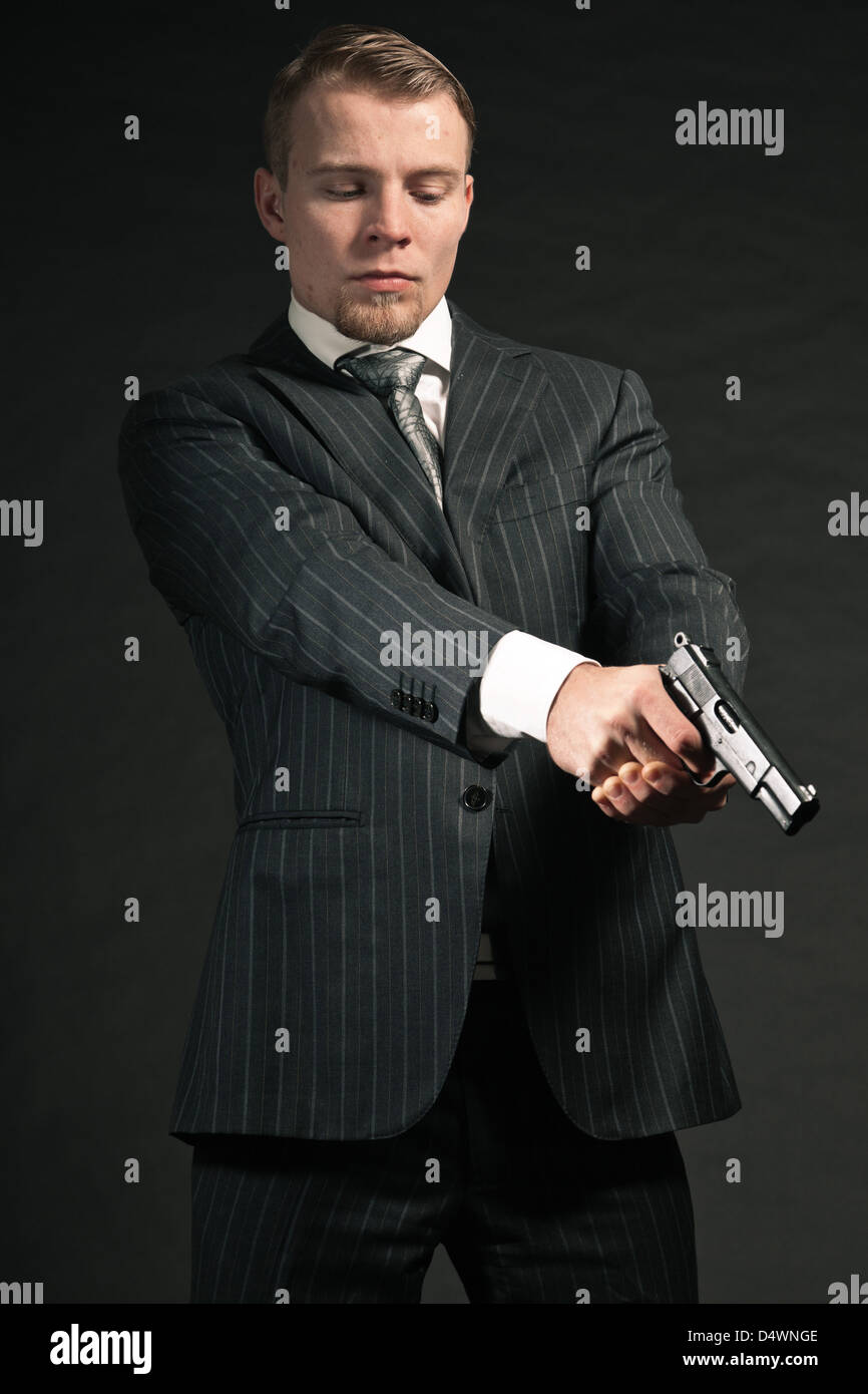 Man in suit shooting with gun. Studio shot against black Stock Photo ...
