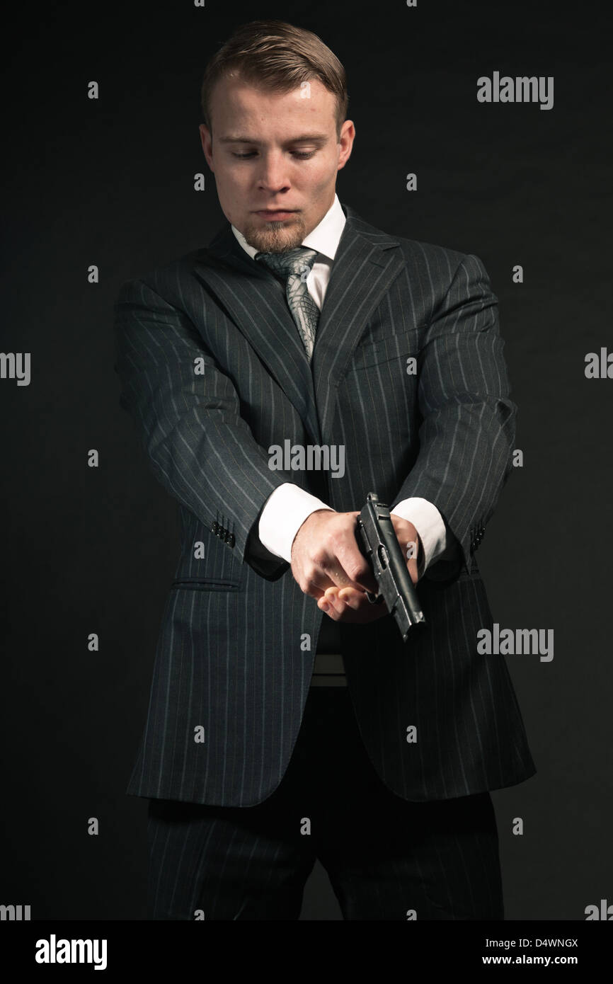 Man in suit shooting with gun. Studio shot against black Stock Photo ...