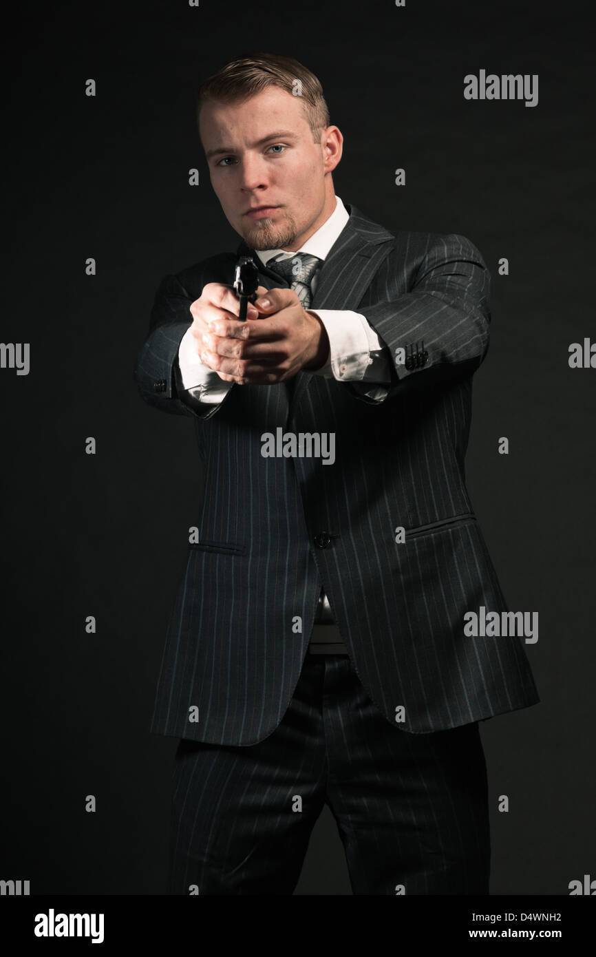 Man in suit shooting with gun. Studio shot against black Stock Photo ...