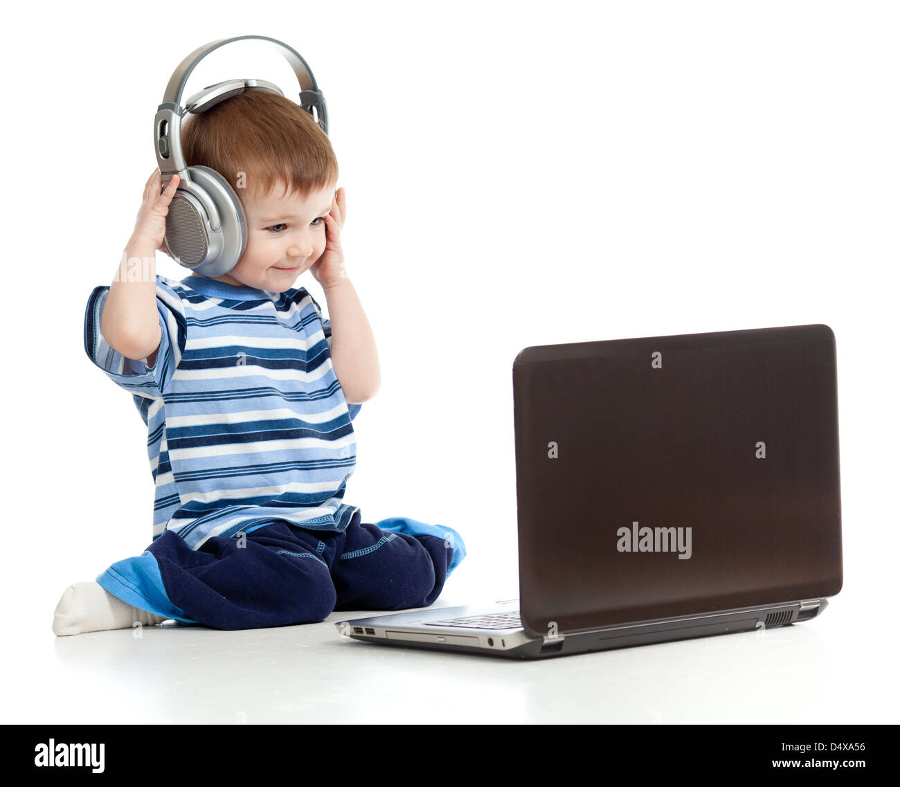 Funny child playing with laptop and listening to music in headphones ...