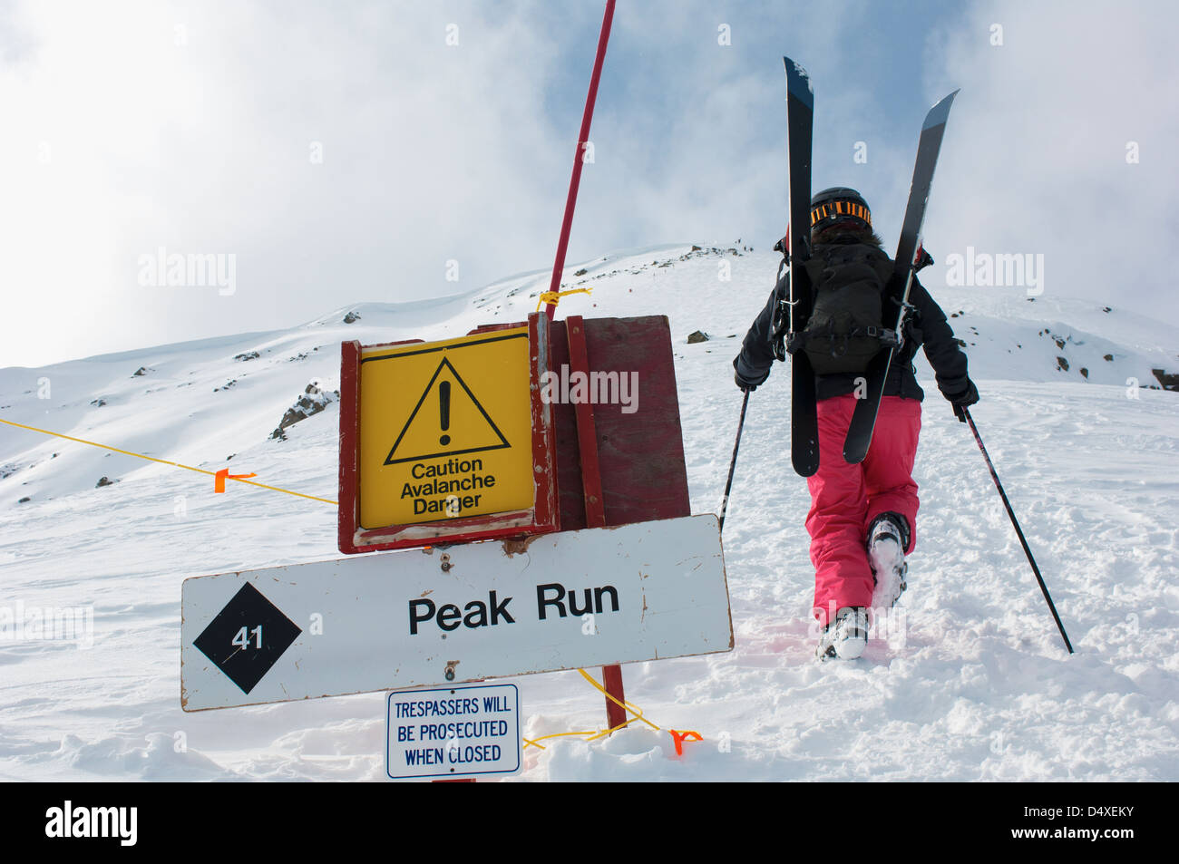 Female skier hikes snow slope with skis on her back in the ski resort ...