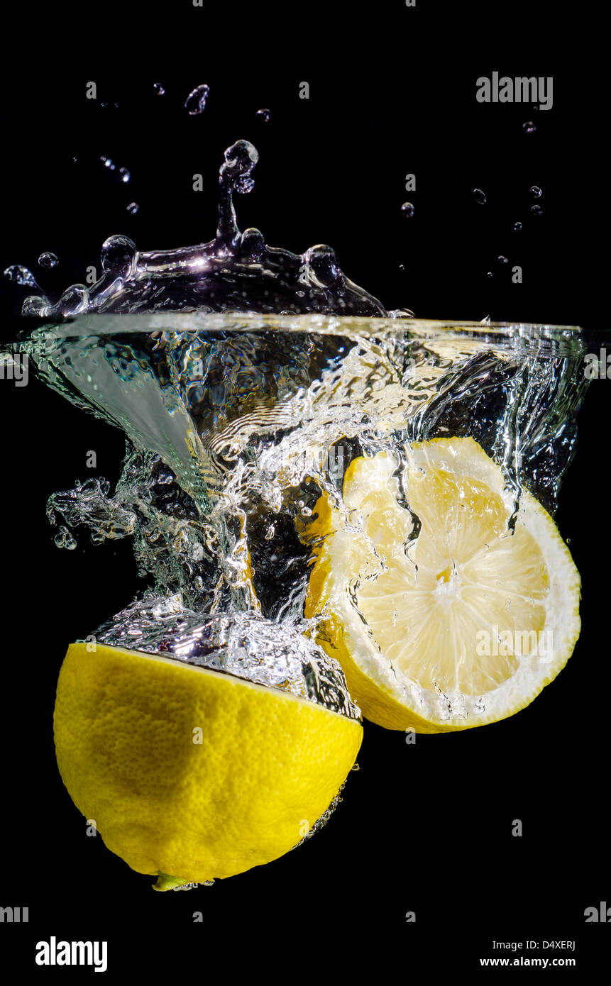 two halved lemons splash into water before black background Stock Photo - Alamy