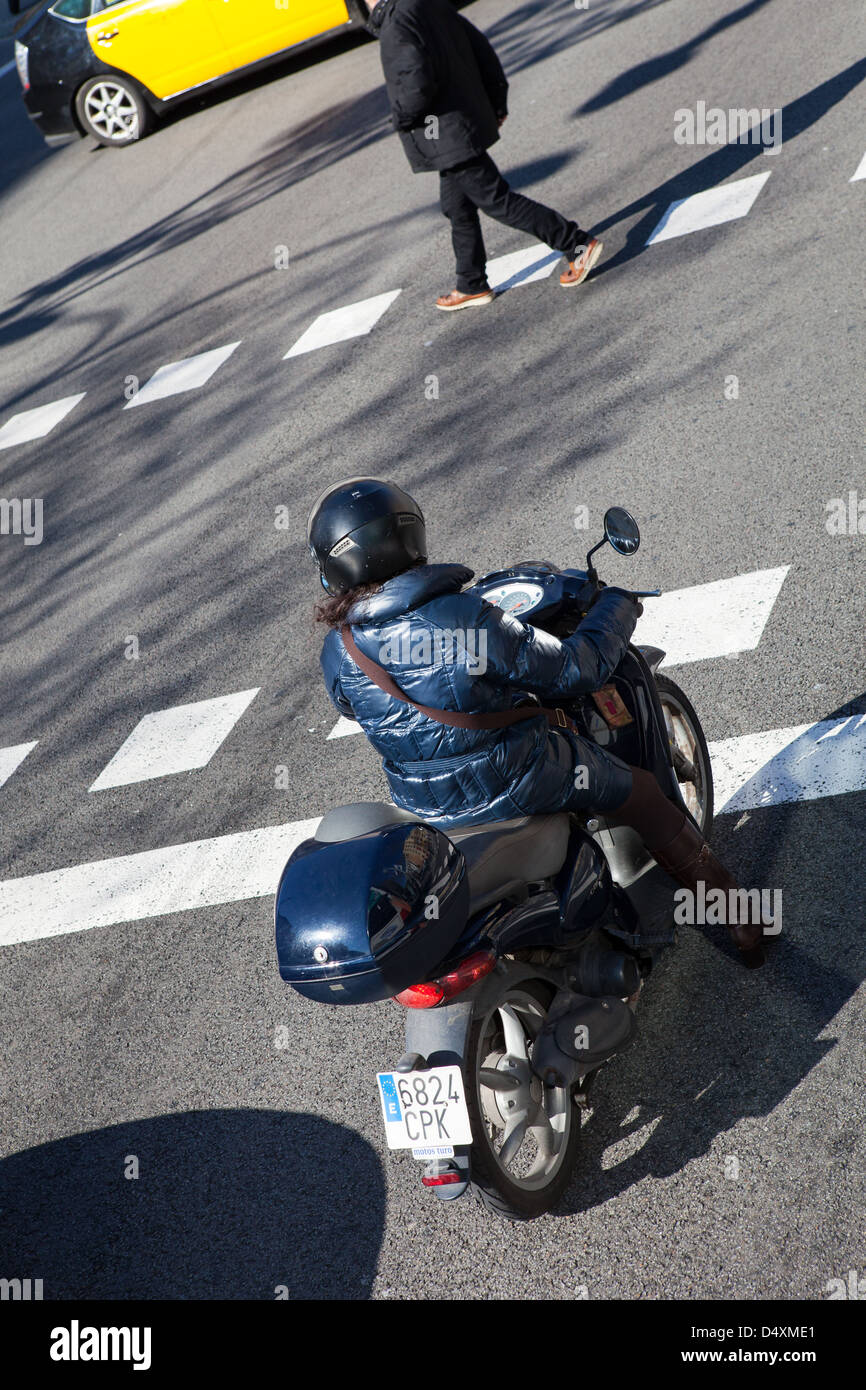A woman riding a motor scooter waits at a red traffic light in downtown ...
