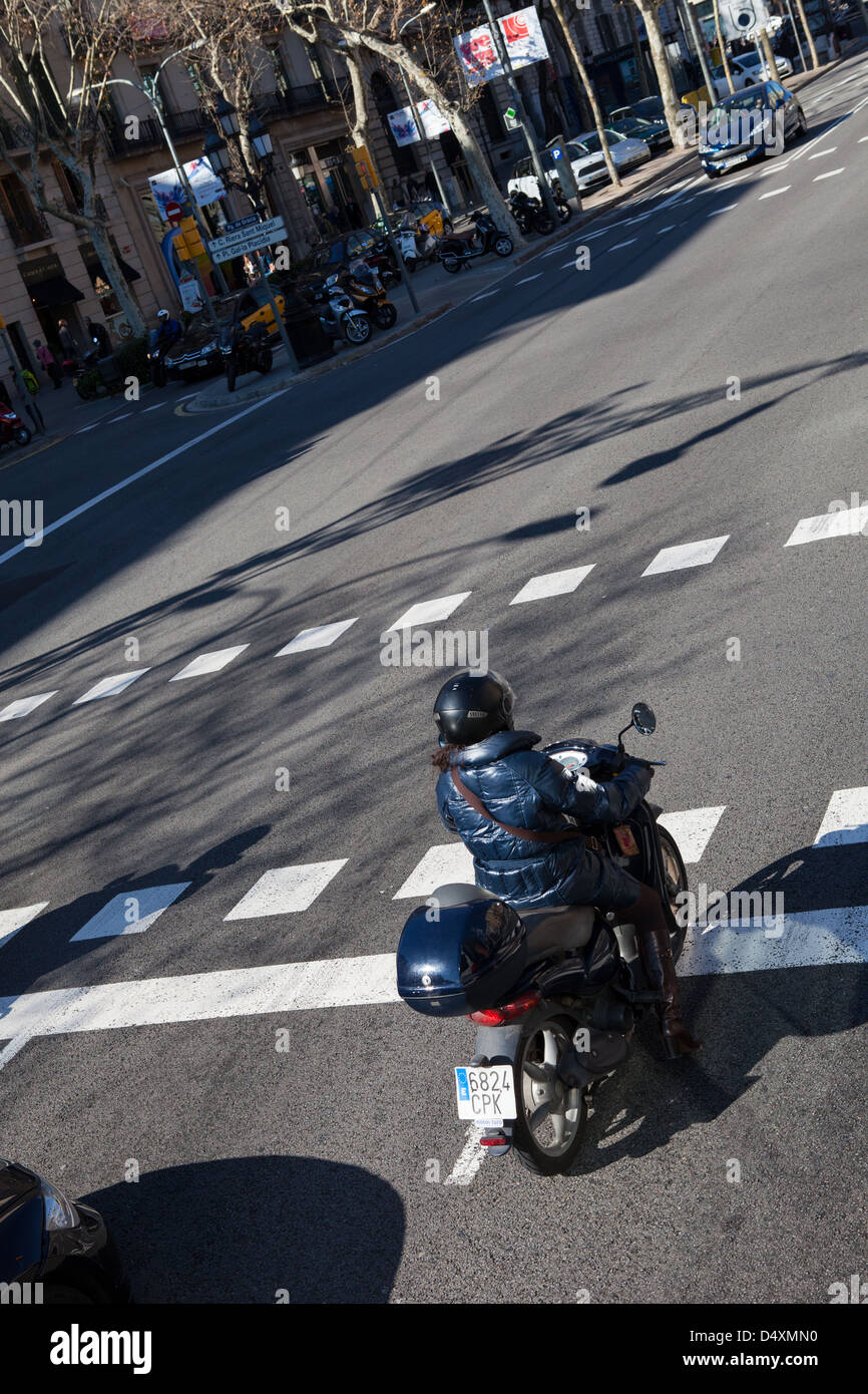 A woman riding a motor scooter waits at a red traffic light in downtown ...