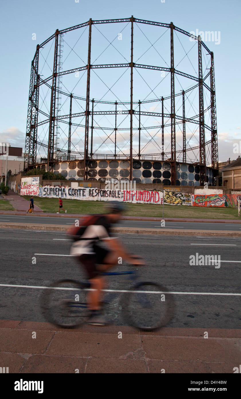Man cycling along the rambla coastal road with gasworks in background ...