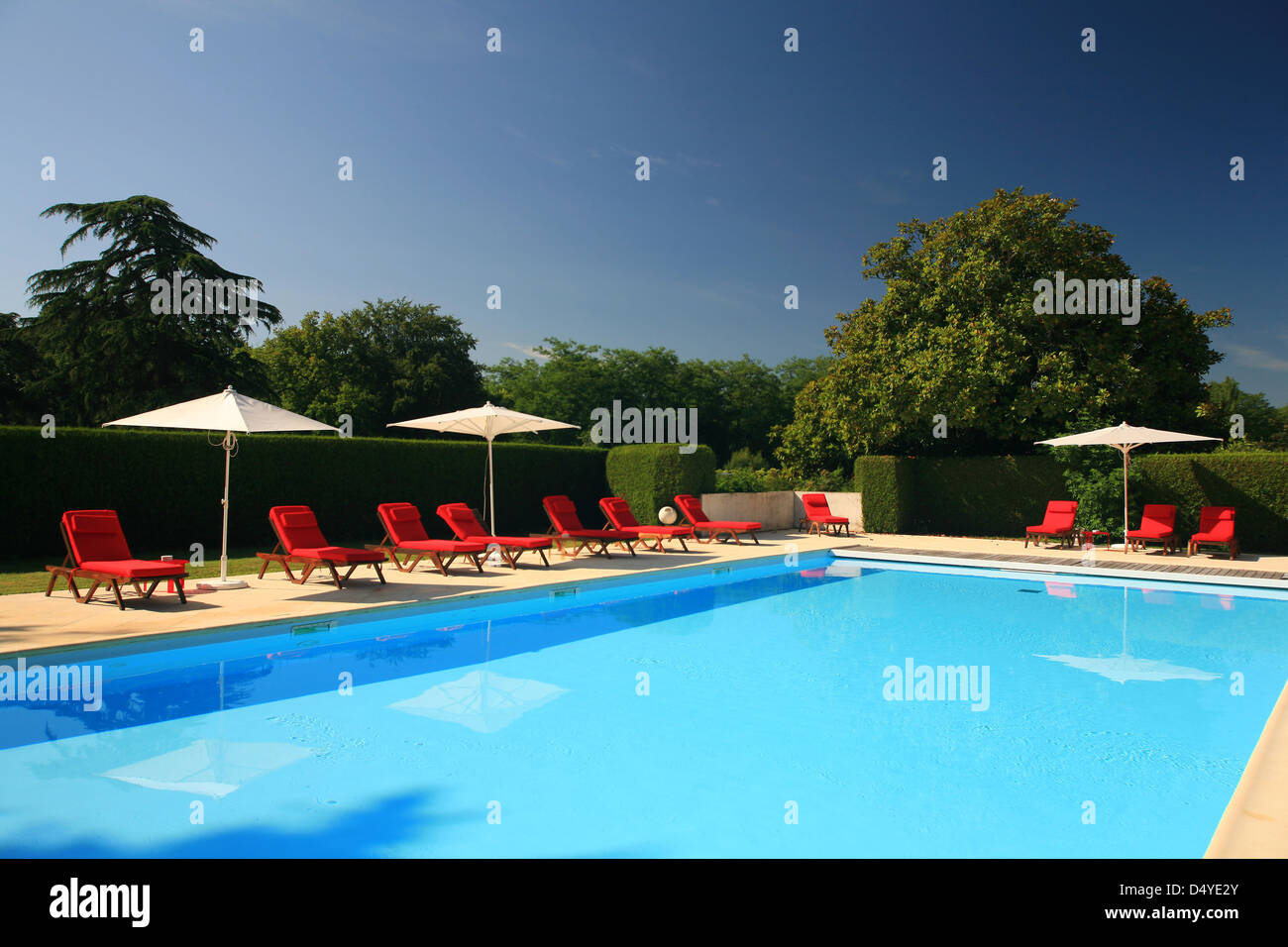 Bright blue swimming pool under deep blue sky with red loungers and ...