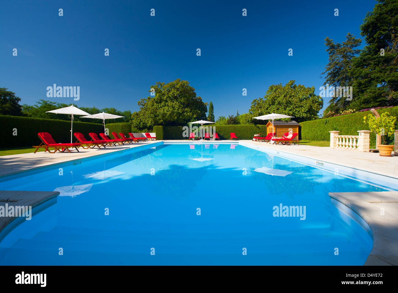 Bright blue swimming pool under deep blue sky with red loungers and ...