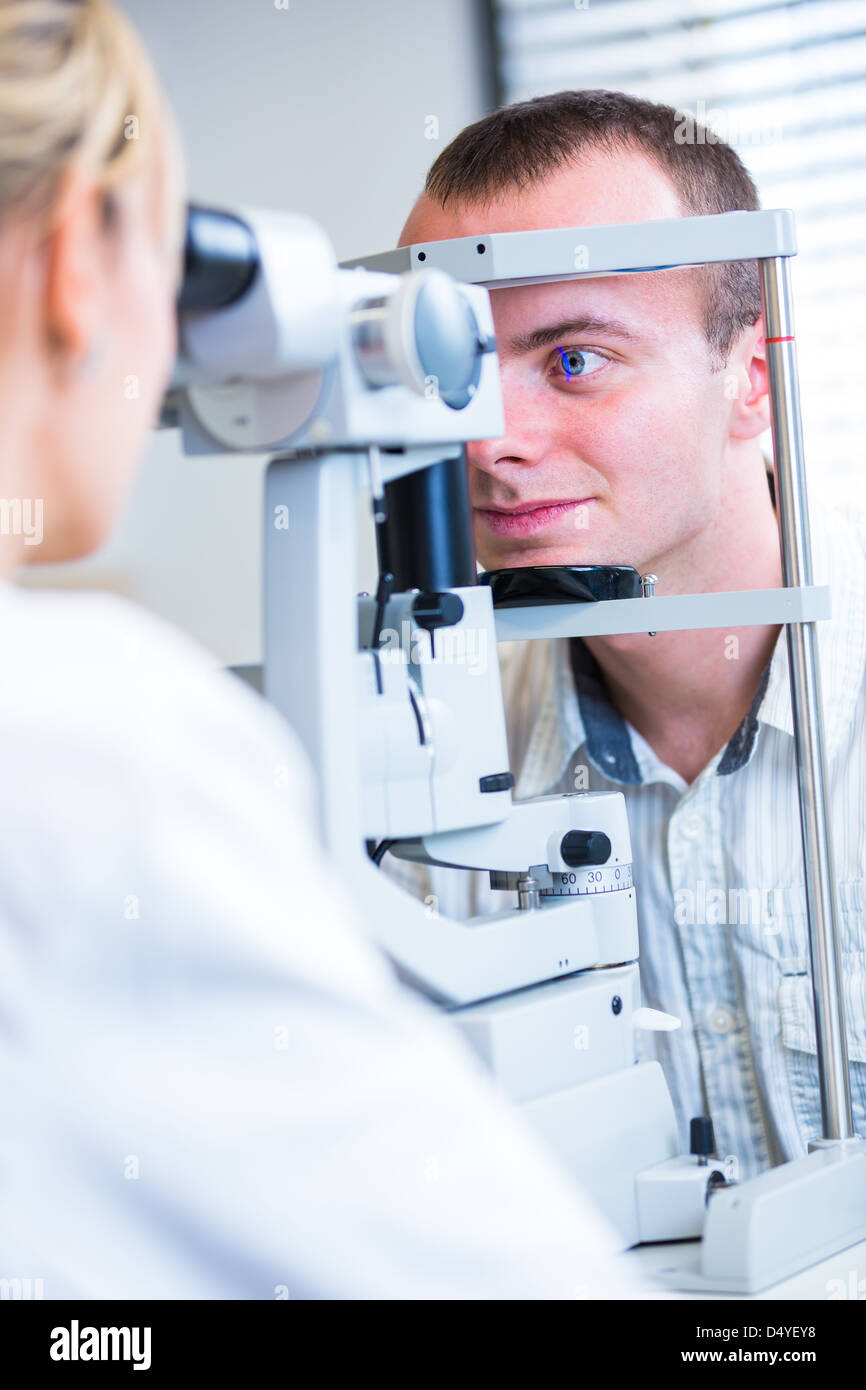 Optometry concept - handsome young man having his eyes examined by an ...