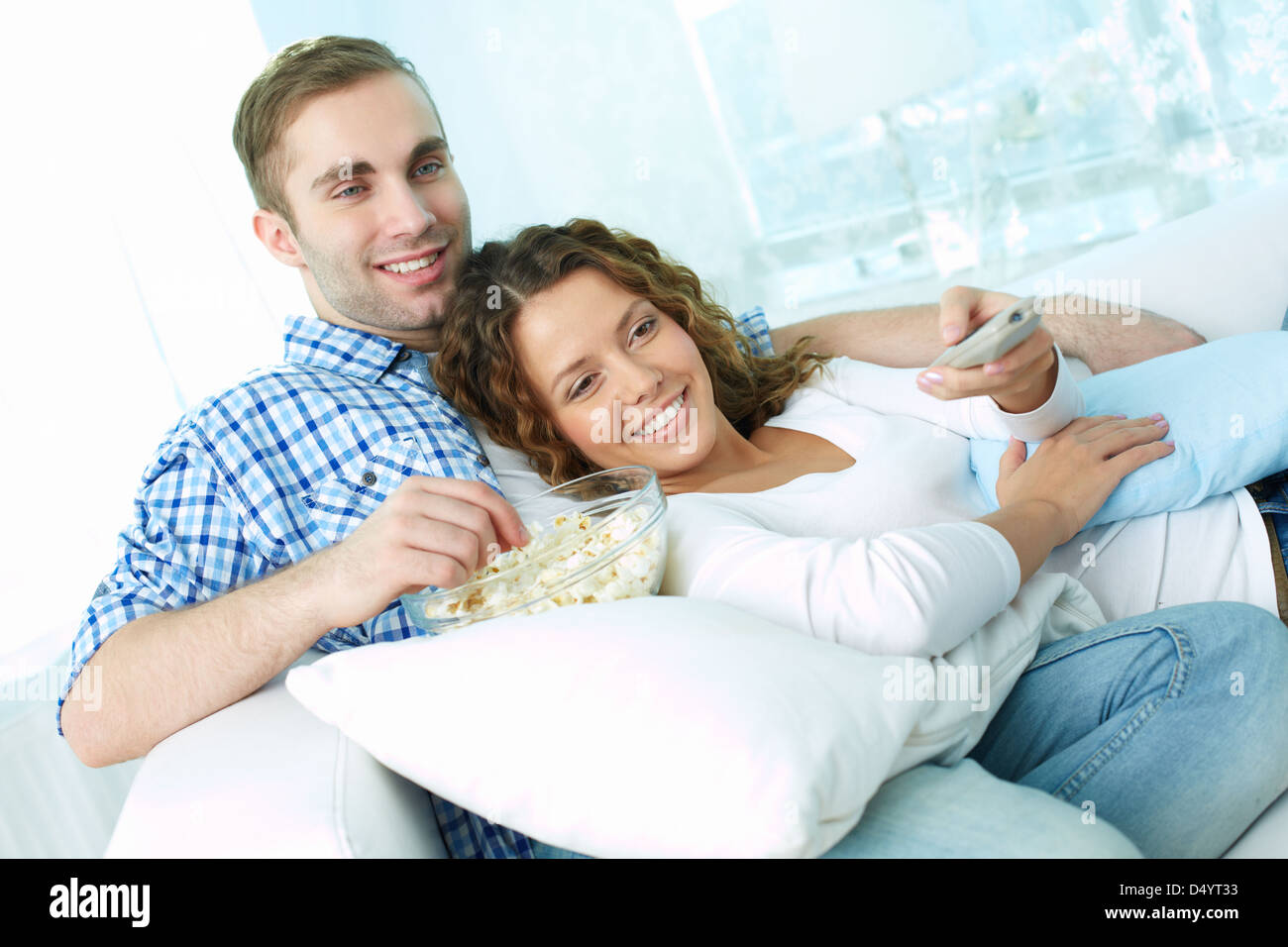 Young lovers enjoying lazy weekend watching TV and eating pop-corn ...