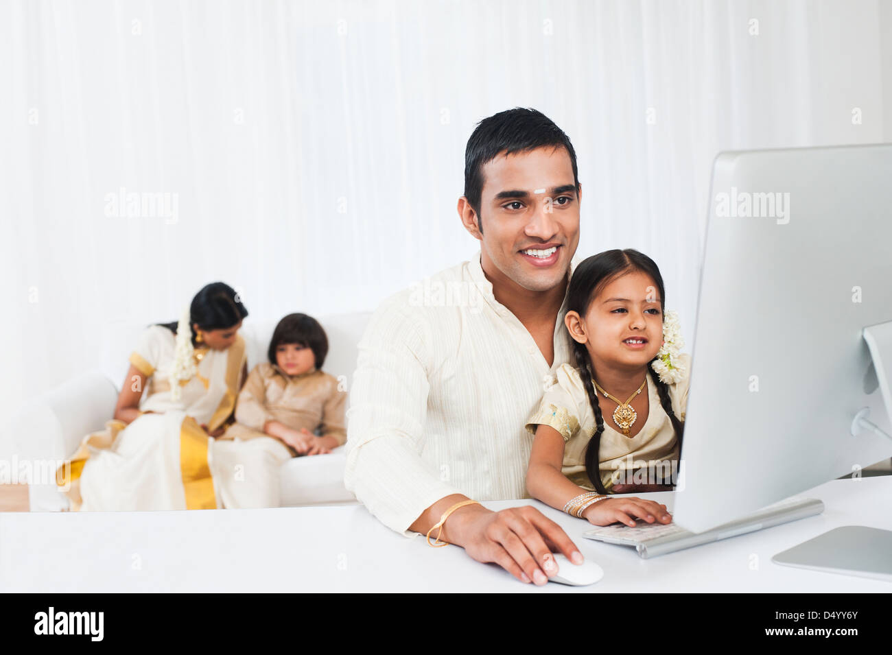 South Indian man using a desktop computer with his daughter with other ...