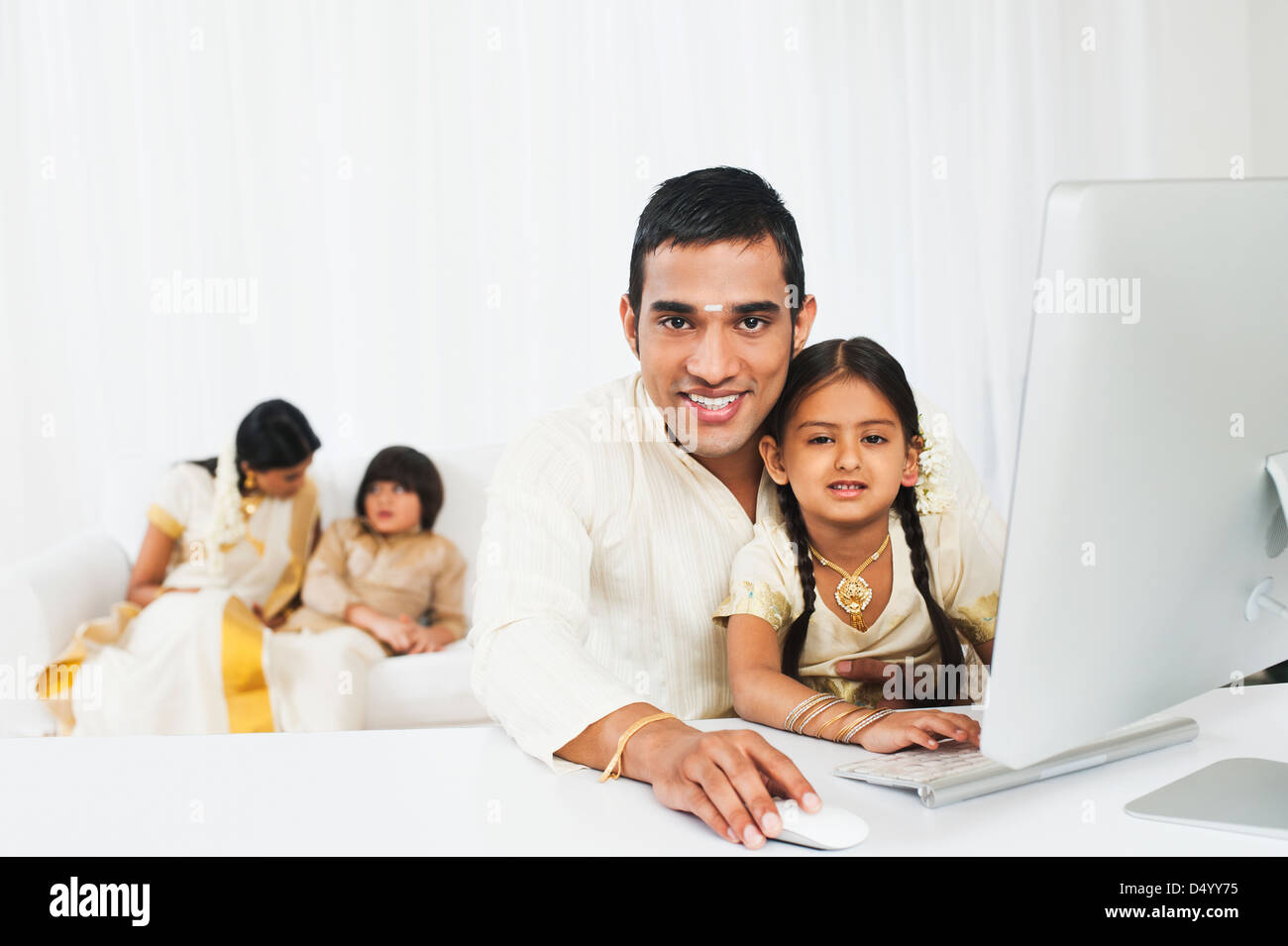 South Indian man using a desktop computer with his daughter with other ...