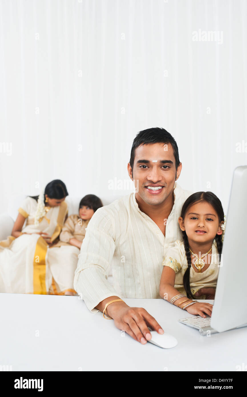 South Indian man using a desktop computer with his daughter with other ...
