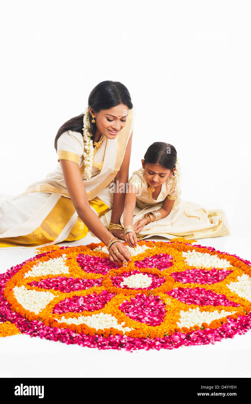 South Indian woman making a rangoli of flowers with her daughter at ...