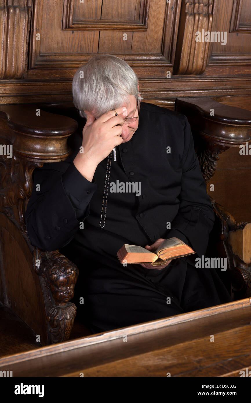 Vintage priest dressed in black cassock reading and holding a rosary ...