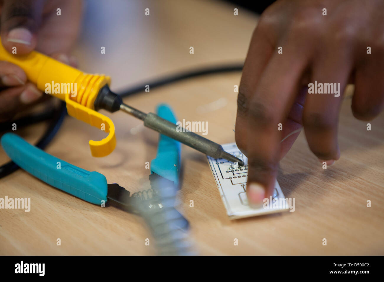A student solders a circuit board during there electronics course at ...