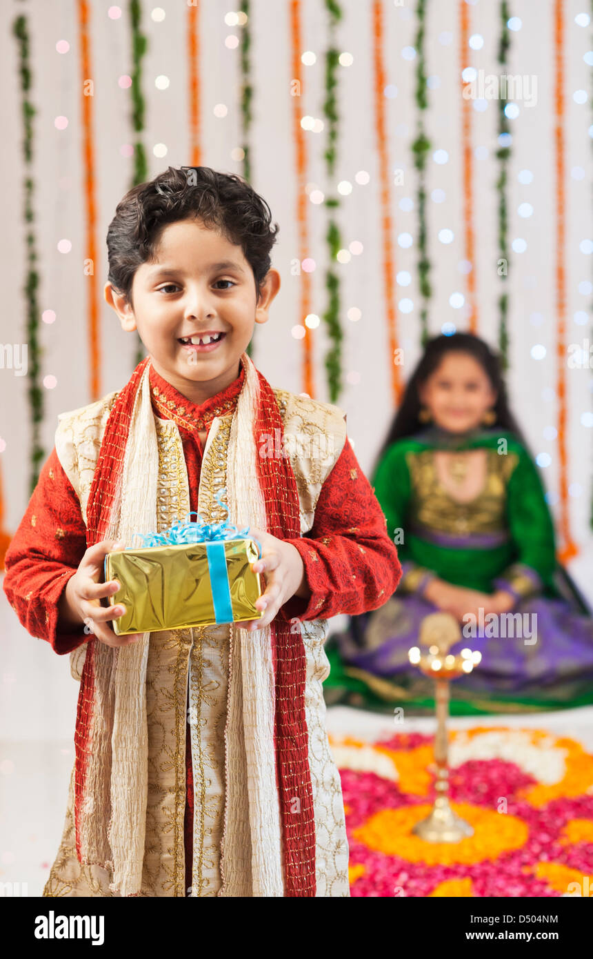 Boy holding a gift with his sister in the background on Diwali Stock ...