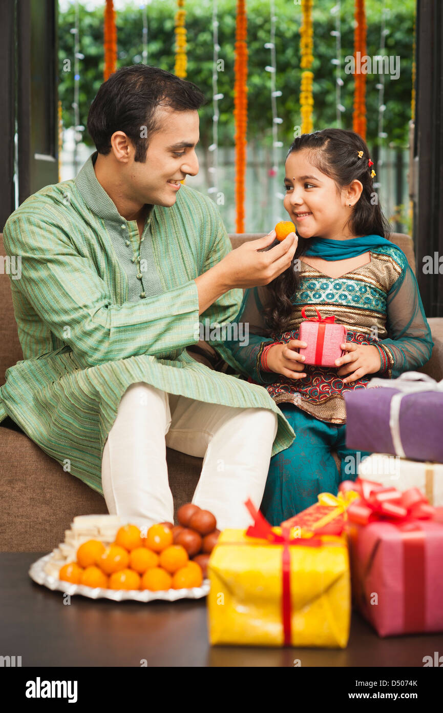 Man feeding laddoo to his daughter on Diwali Stock Photo - Alamy