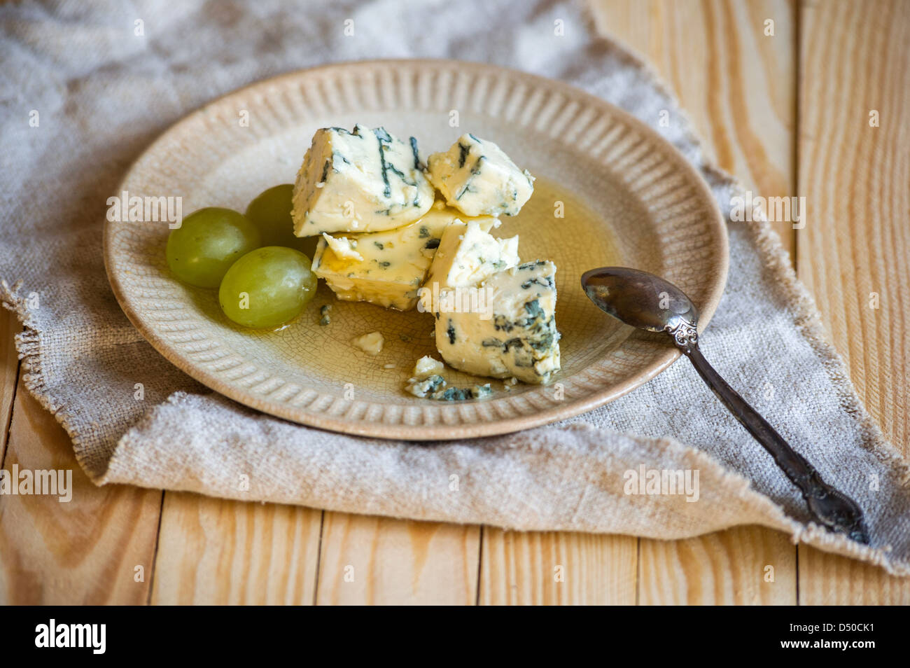 Close-up of blue mold cheese and grapes on a plate. Wooden background ...