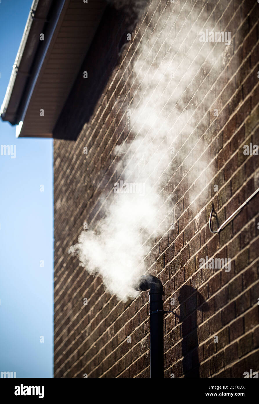 Steam rising from a central heating boiler outlet flue pipe on a winter ...