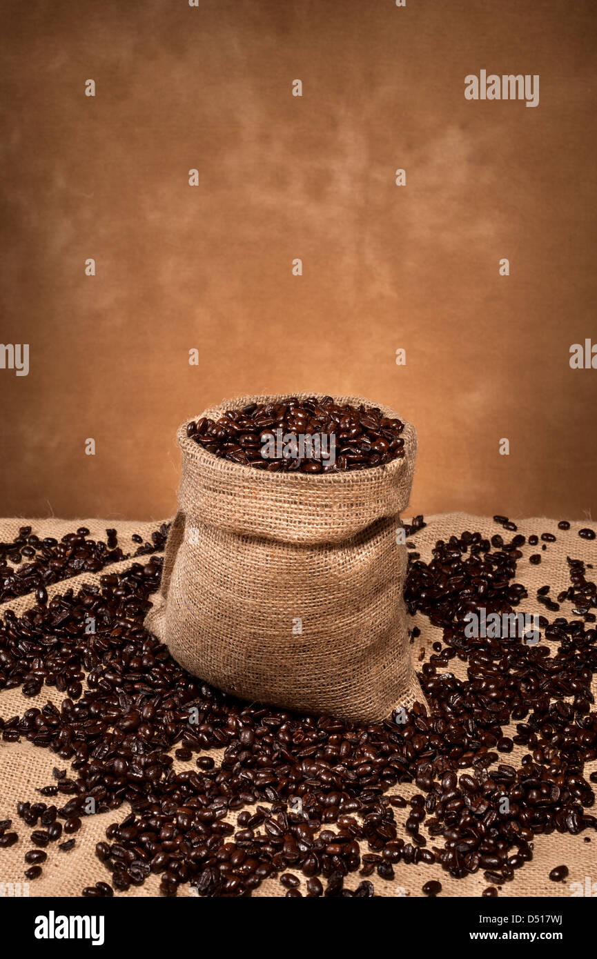 A burlap sack filled with coffee beans and surrounded with spilled ...