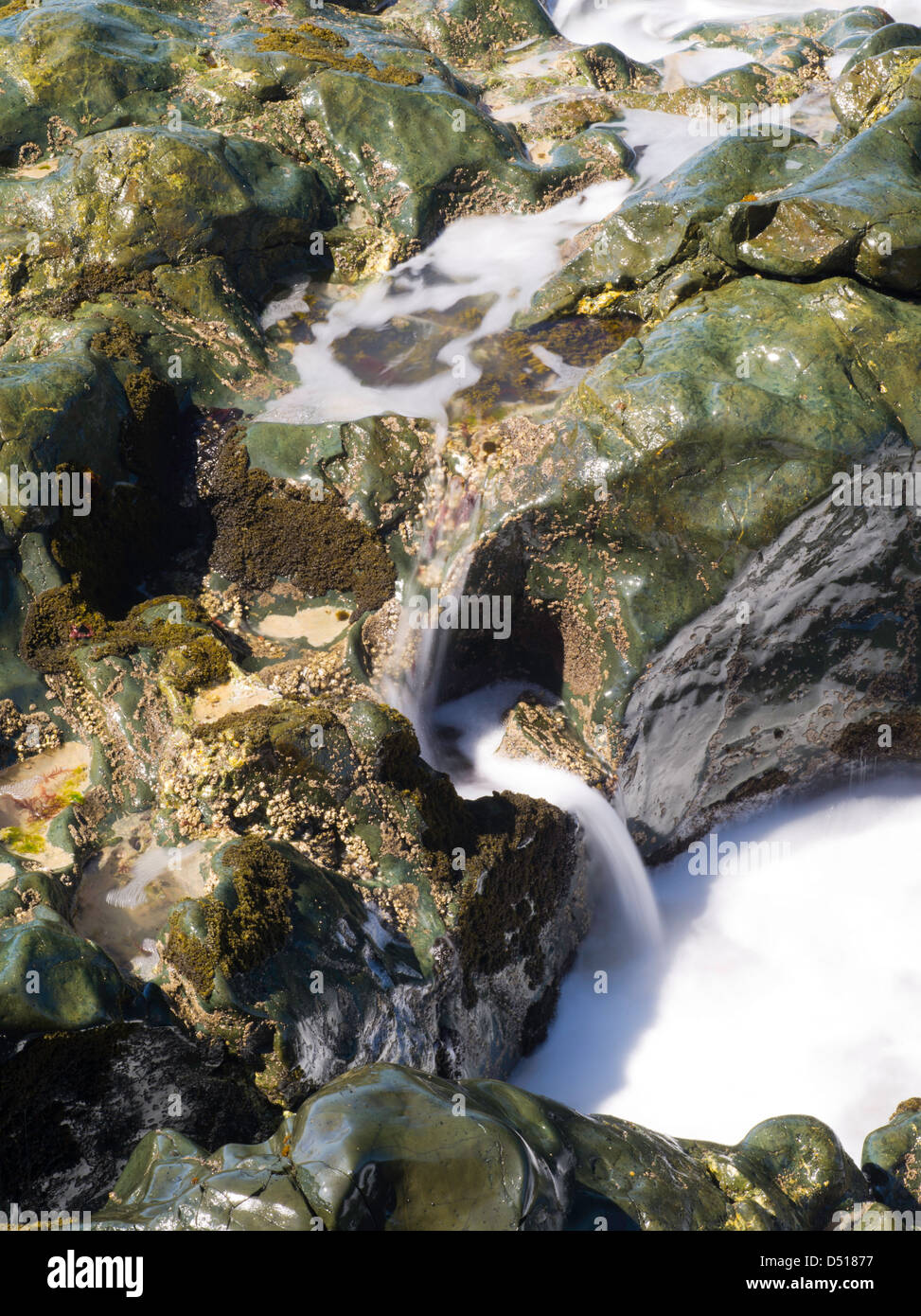 Waves crash on sea-side rocks, slowly carving the rock and creating ...